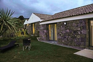 Um edifício de pedra com telhado de telhas, janelas grandes e um gramado com móveis de jardim.