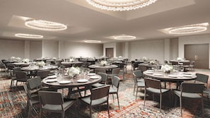 Uma grande sala de conferências com várias mesas redondas, cada uma disposta com pratos, copos e centros de mesa florais.