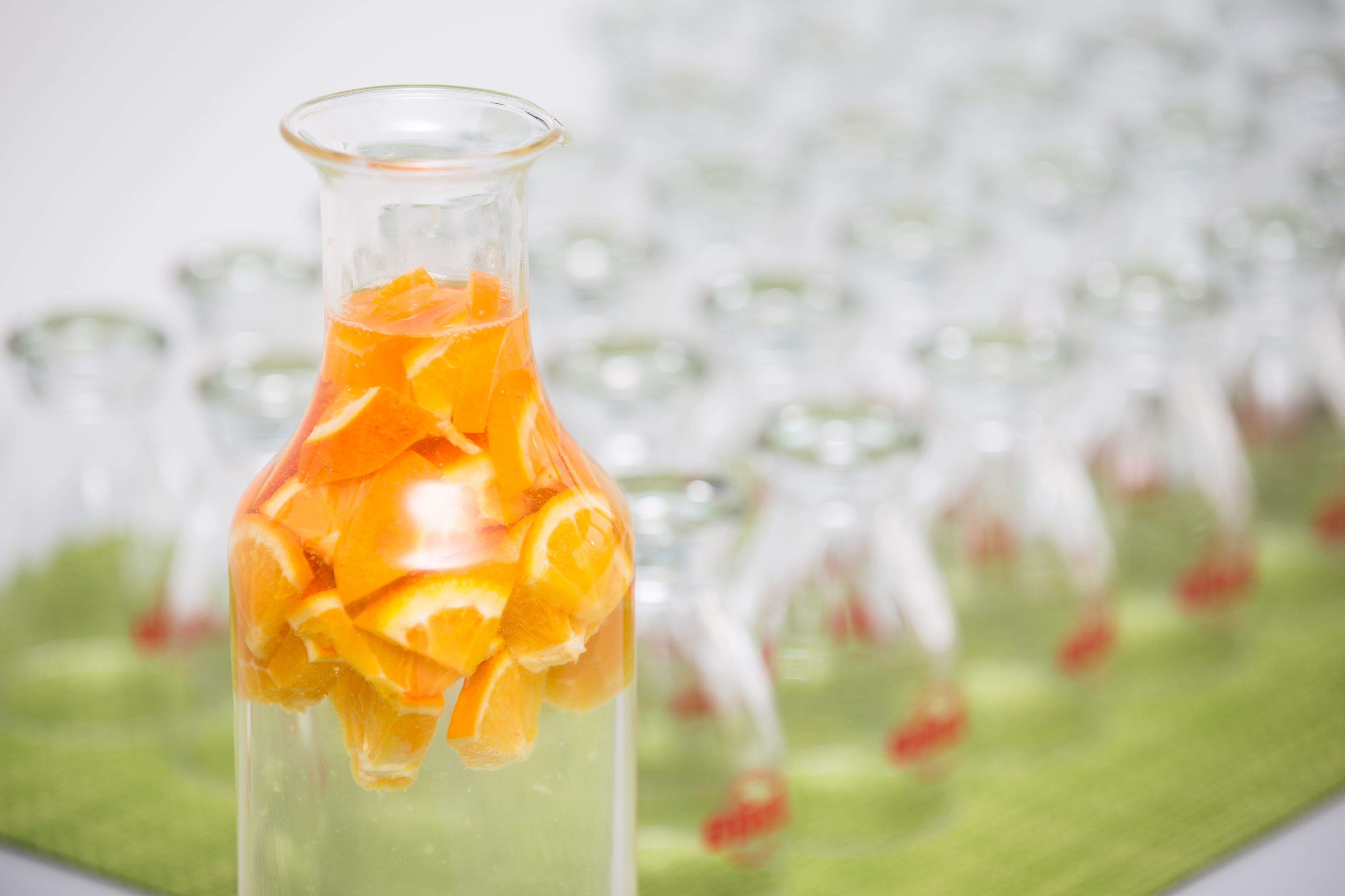 Um frasco de laboratório com fatias de laranja e água, rodeado por frascos vazios sobre uma superfície verde.