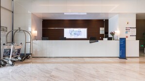 Uma área de recepção de hotel com design moderno, incluindo um balcão de atendimento, uma tela digital e um piso limpo revestido de azulejos.