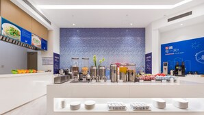 Um lobby de hotel moderno com um balcão central exibindo diversas comodidades, incluindo uma máquina de café, chaleiras e uma seleção de frutas.