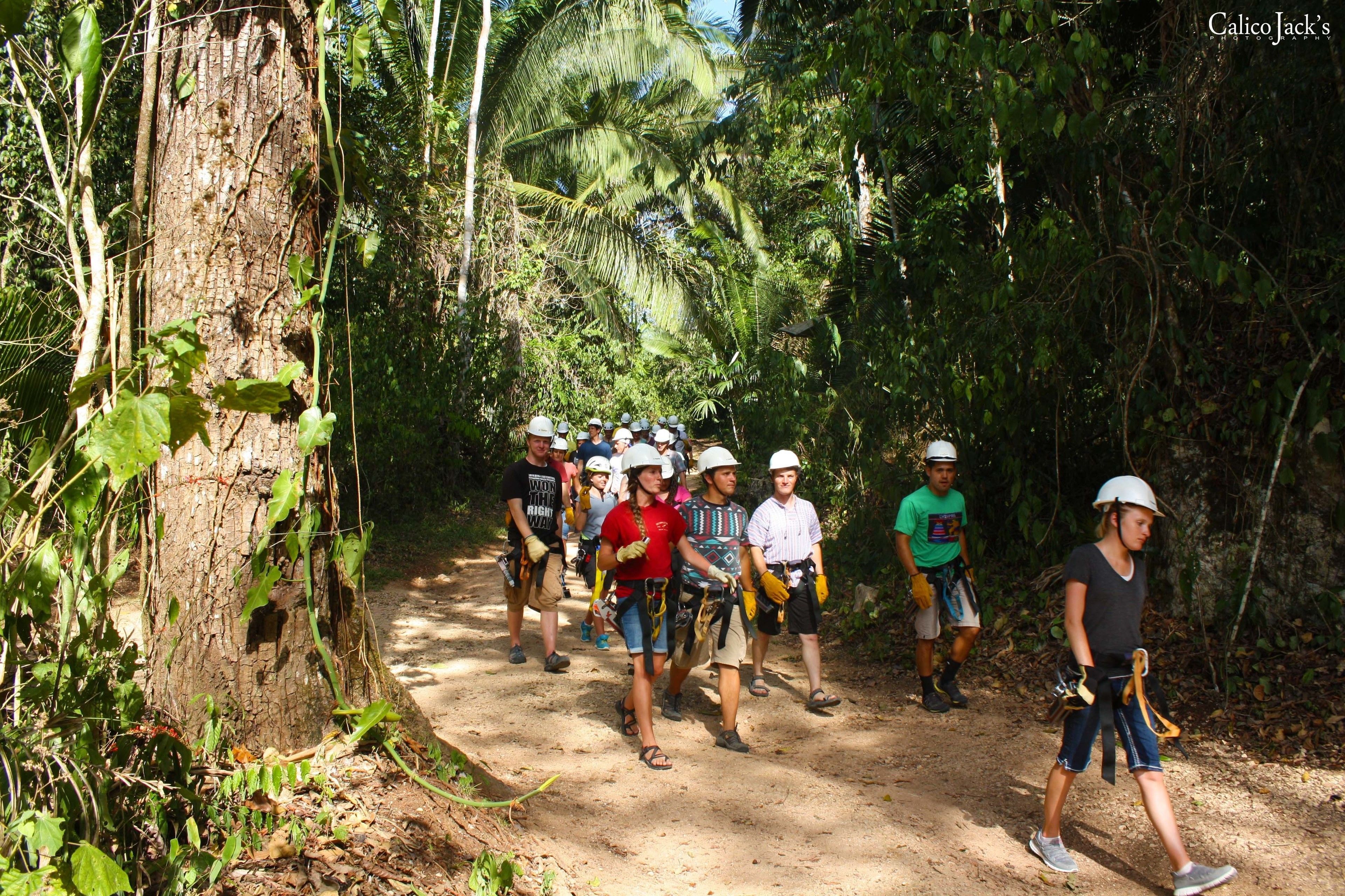 Um grupo de pessoas caminhando por uma trilha de terra em meio a vegetação densa e árvores.