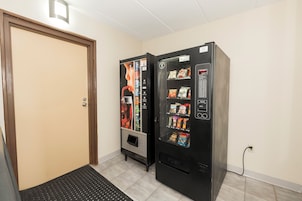 Um quarto com porta, máquina de vendas de lanches e uma lixeira.
