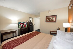 Quarto de hotel com cama, escrivaninha, televisão, cafeteira e quadro na parede.