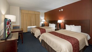 Quarto de hotel com duas camas, uma mesa de escritório com um laptop, uma televisão e uma janela grande com cortinas.