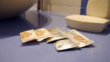 Quatro embalagens de um produto em uma bancada de banheiro, ao lado de um saboneteira.