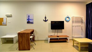 Quarto com televisão, mobiliário de madeira, parede branca com quadro e cortina azul.