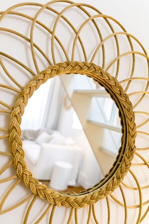 Espelho circular trançado com moldura geométrica, refletindo um quarto com cama e janela.