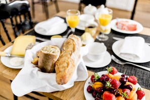 Café da manhã com pão, frutas e suco de laranja sobre uma mesa de madeira.