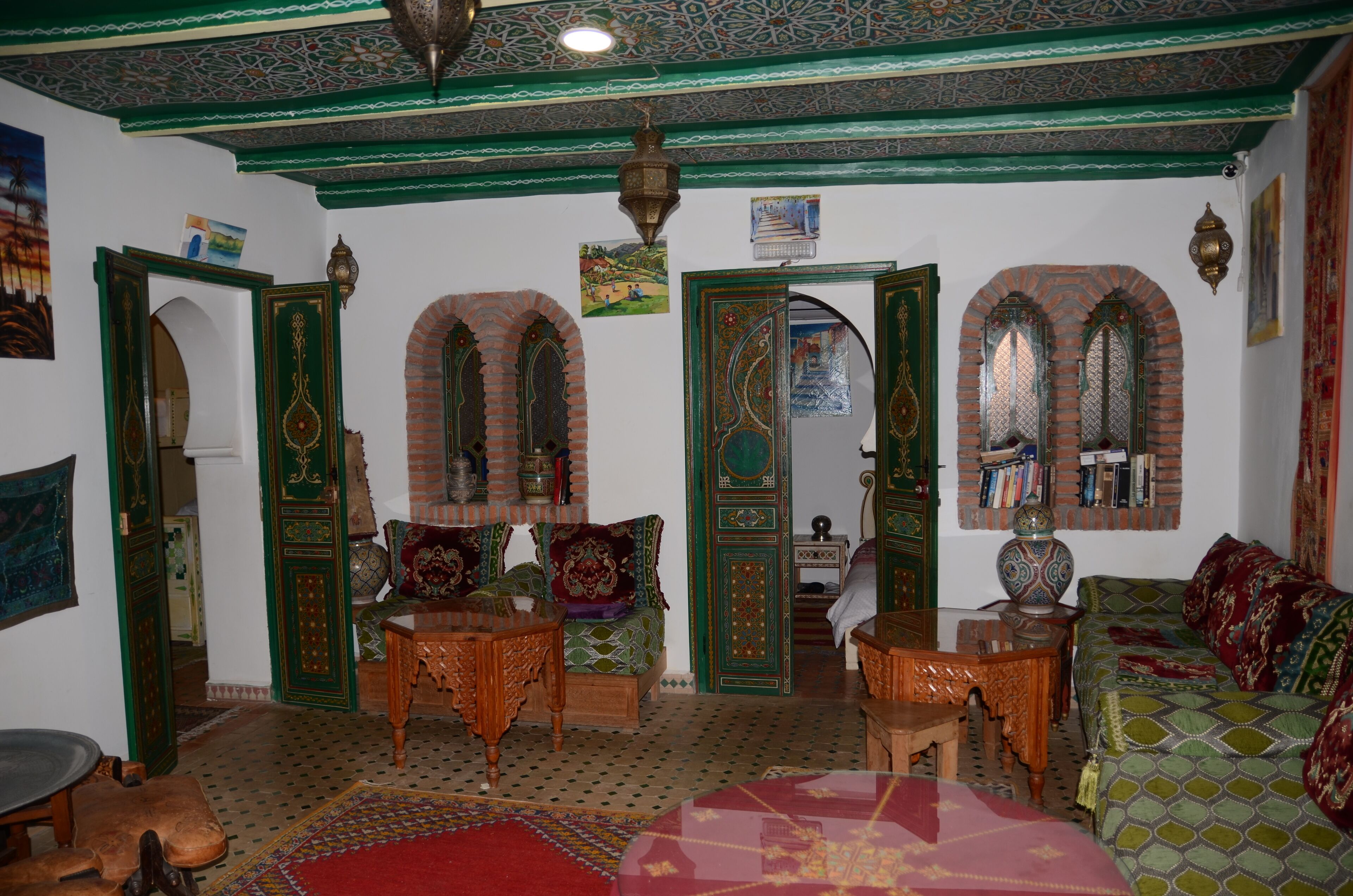 Um quarto tradicional marroquino com portas verdes ricamente decoradas, um tapete estampado e uma mesa de centro de madeira.