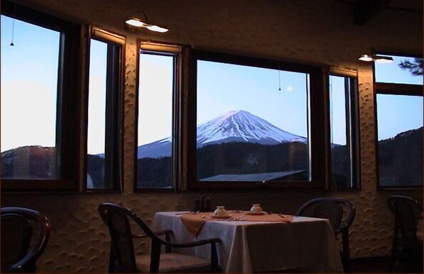 Uma área de refeições com uma mesa posta para dois, janelas amplas com vista para uma montanha nevada e uma parede com textura.