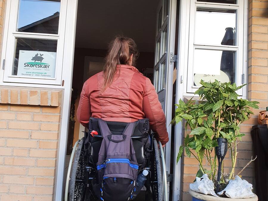 Uma pessoa em cadeira de rodas saindo de um prédio por uma porta.