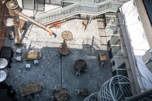Um terraço ao ar livre com mesas e cadeiras redondas, uma escadaria de metal e uma grande escultura metálica.