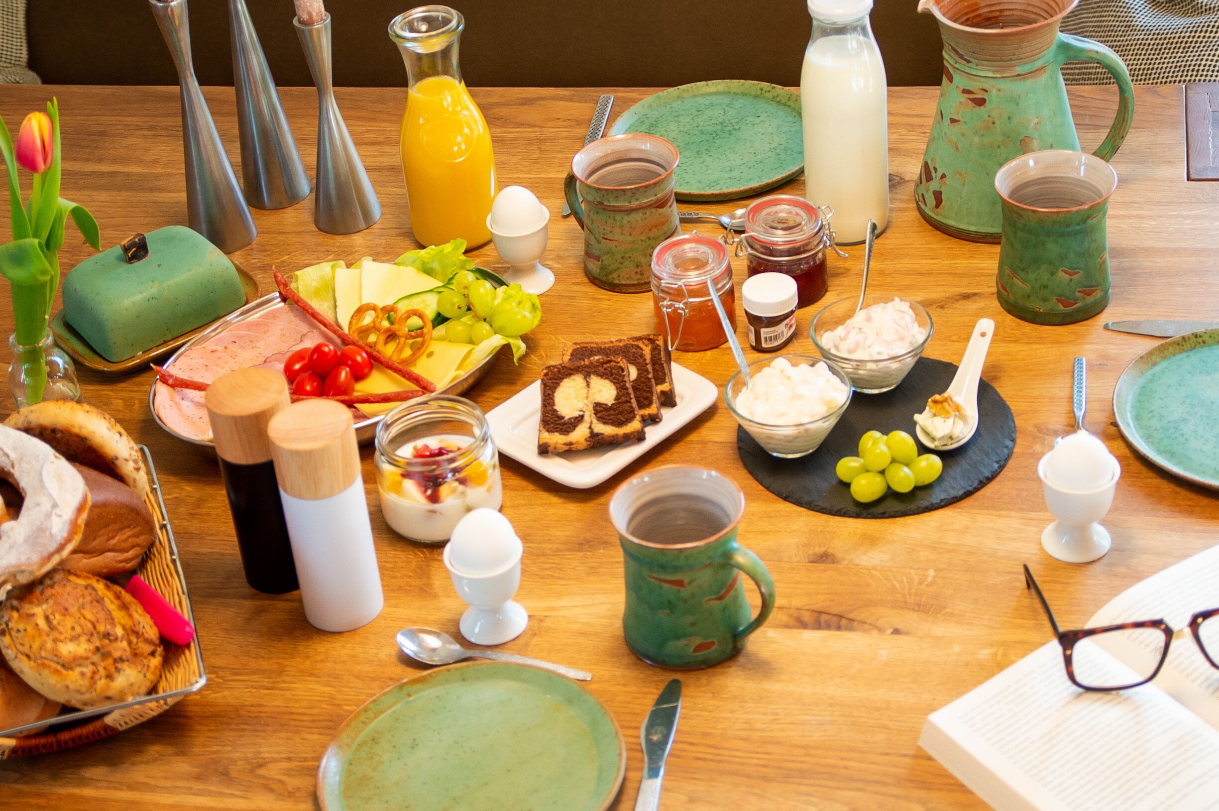 Mesa de café da manhã com diversos alimentos, utensílios e recipientes.