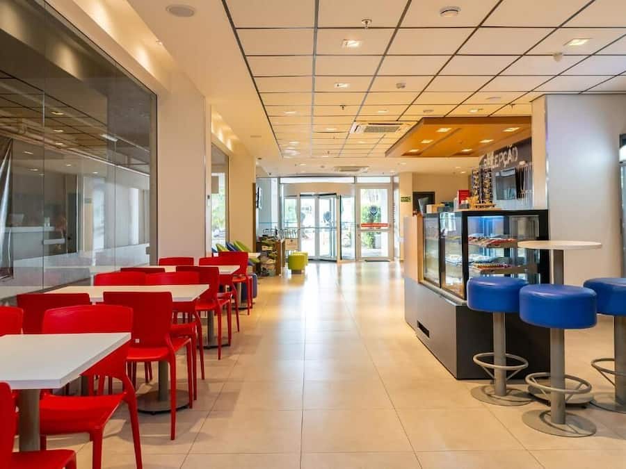 Decoração moderna com cadeiras e mesas vermelhas, área de bar com banquetas e vista para o exterior através de grandes janelas.