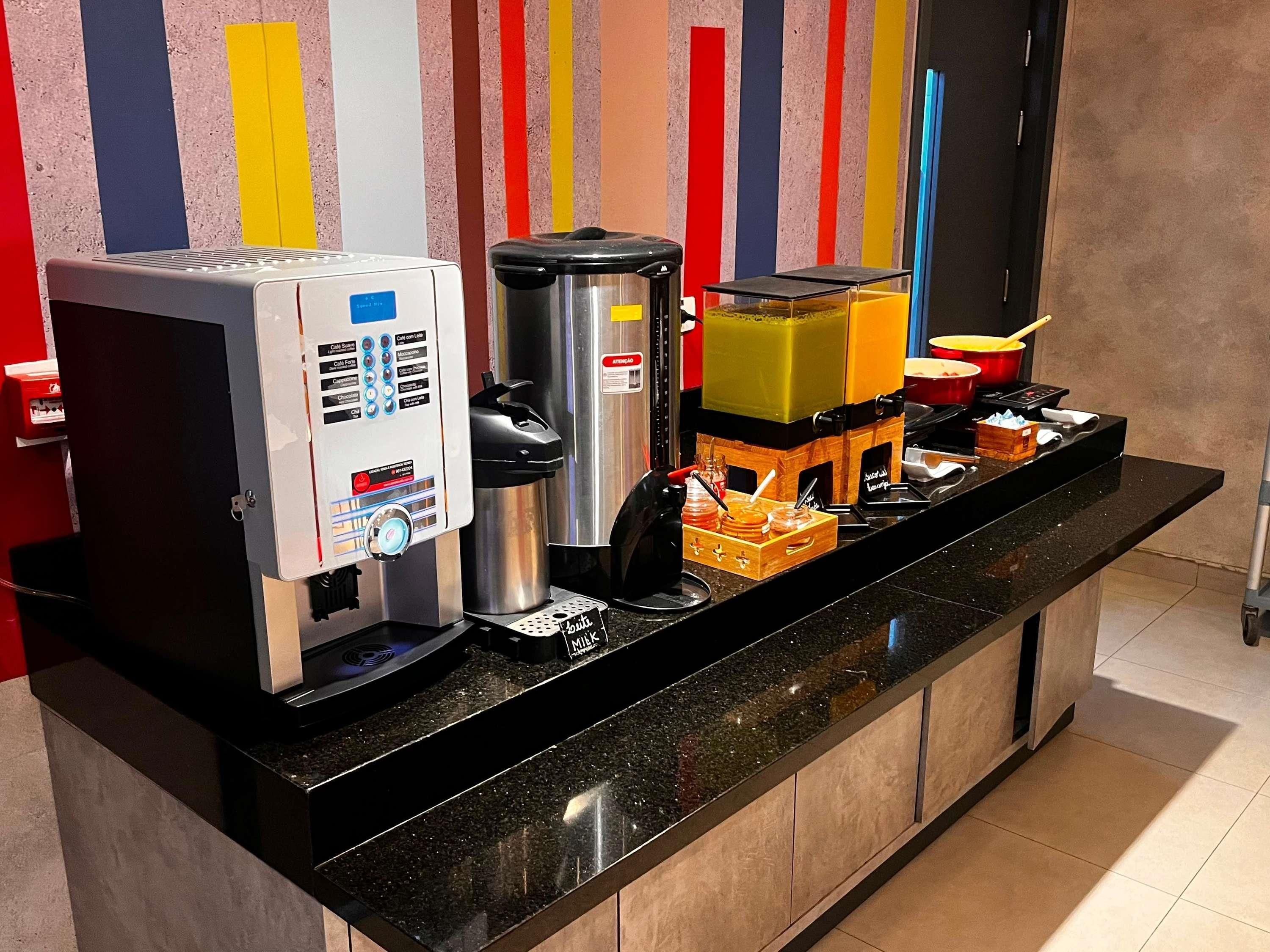 Um espaço com estação de café, incluindo uma cafeteira, um dispensador de água quente e uma prensa francesa.