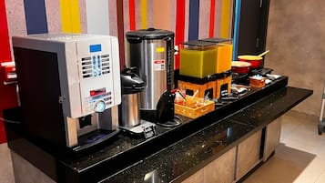 Um espaço com estação de café, incluindo uma cafeteira, um dispensador de água quente e uma prensa francesa.