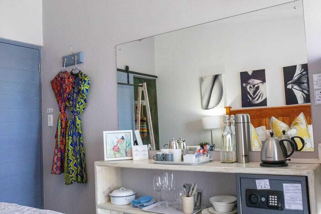 Quarto de hotel com cama, espelho, uma mesinha com chaleira, xícaras e porta-retrato.
