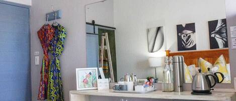 Quarto de hotel com cama, espelho, uma mesinha com chaleira, xícaras e porta-retrato.