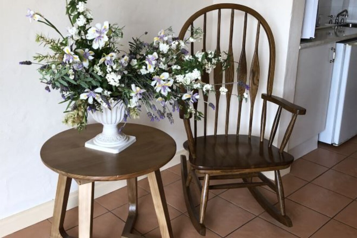 Uma cadeira de madeira e uma pequena mesa redonda com um vaso branco com flores.