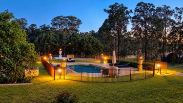 Piscina com cerca ao redor, cadeiras de descanso e uma fonte.
