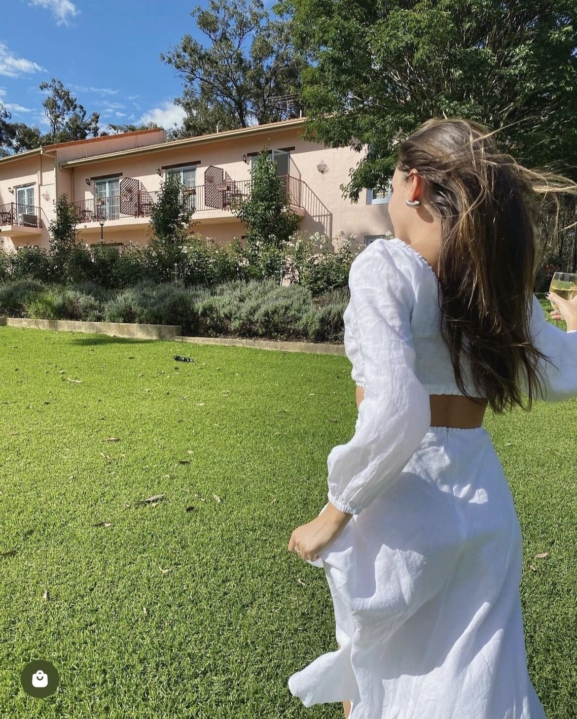 Uma pessoa vestida de branco está em um gramado com uma casa ao fundo.