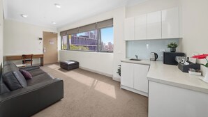 Um apartamento moderno com cozinha compacta, sofá, área de jantar e uma grande janela com vista para a cidade.