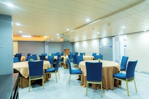 Sala de conferências com mesas redondas e cadeiras azuis, equipada com sinalização de saída de incêndio e ponto de acionamento.