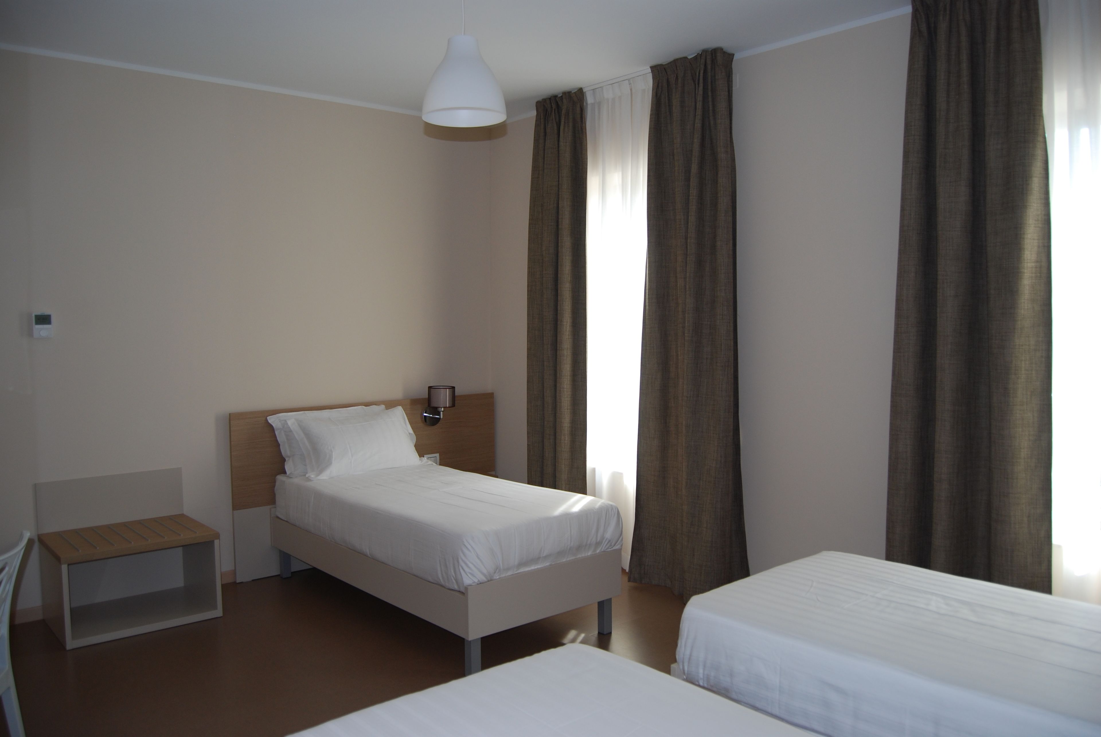 Quarto de hotel com duas camas, uma mesa de cabeceira, uma luminária e uma janela com cortinas.