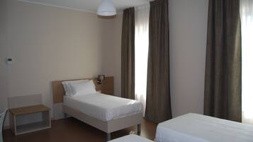 Quarto de hotel com duas camas, uma mesa de cabeceira, uma luminária e uma janela com cortinas.