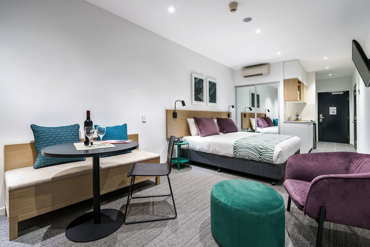 Quarto de hotel moderno com uma cama, um sofá, uma mesa pequena e uma cadeira.