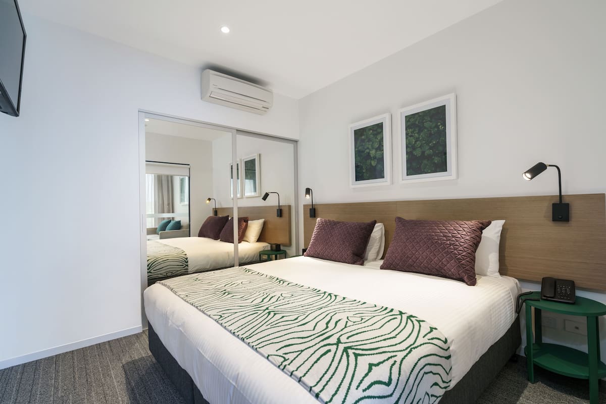 Quarto de hotel com uma cama grande, uma mesinha de cabeceira, um espelho e duas imagens emolduradas na parede.