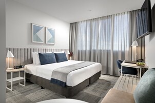 Quarto de hotel moderno com uma cama grande, mesas de cabeceira, uma escrivaninha e uma televisão.