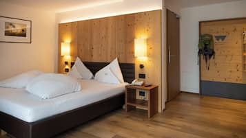 Quarto de hotel moderno com cabeceira de madeira, cama com roupa de cama branca, luminárias laterais, uma pequena mesa de cabeceira de madeira e uma mochila pendurada na parede.
