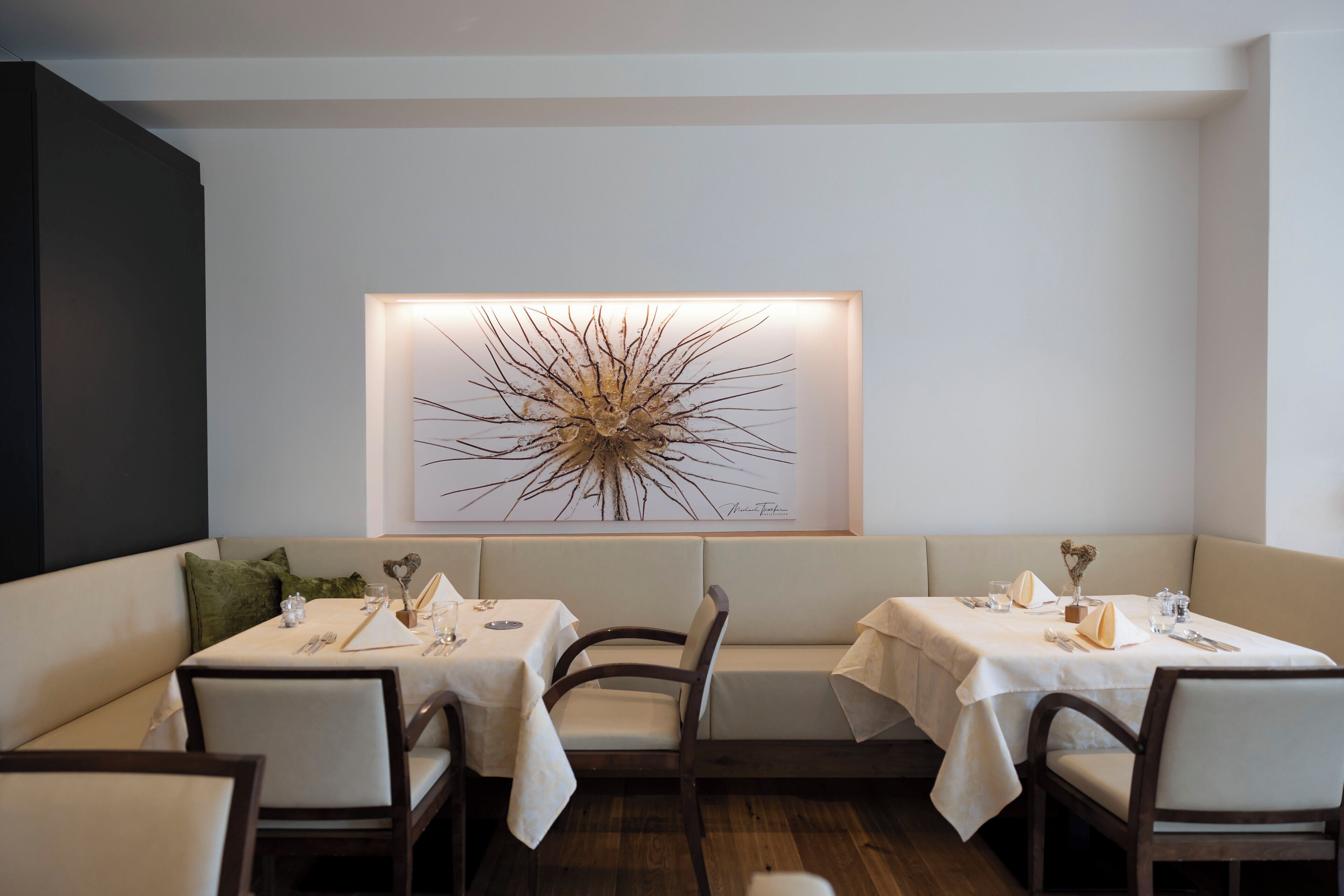 Um restaurante com decoração moderna, apresentando uma grande obra de arte abstrata na parede, mesas organizadas com toalhas brancas e assentos acolchoados.