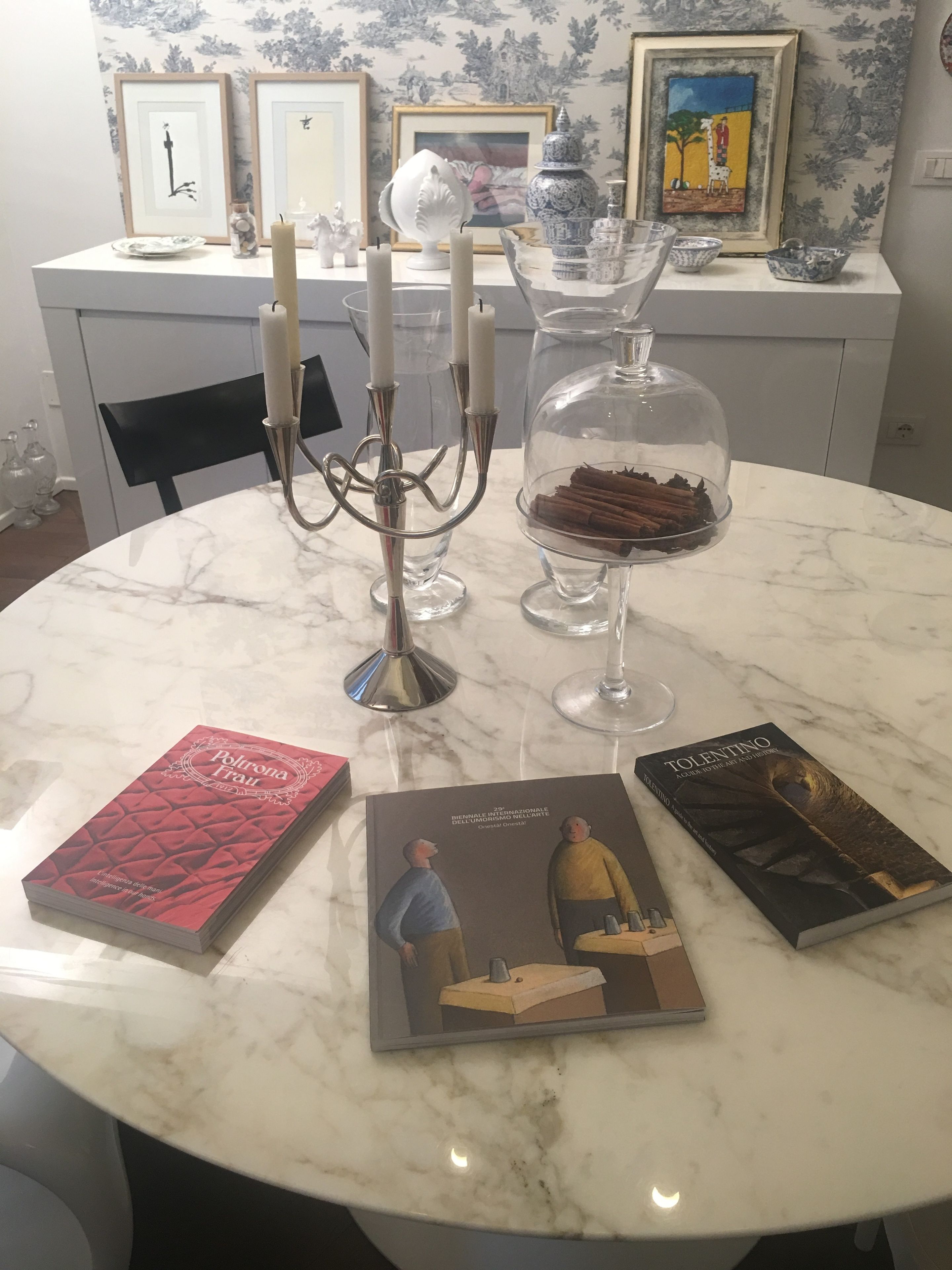 Uma mesa de mármore com livros, um candelabro e uma cúpula de vidro com raspas de chocolate.