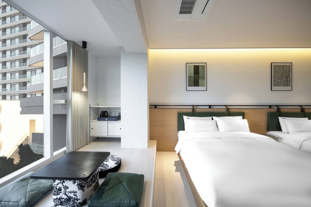Quarto de hotel moderno com uma cama grande, um pequeno espaço de estar e vista para a paisagem urbana.