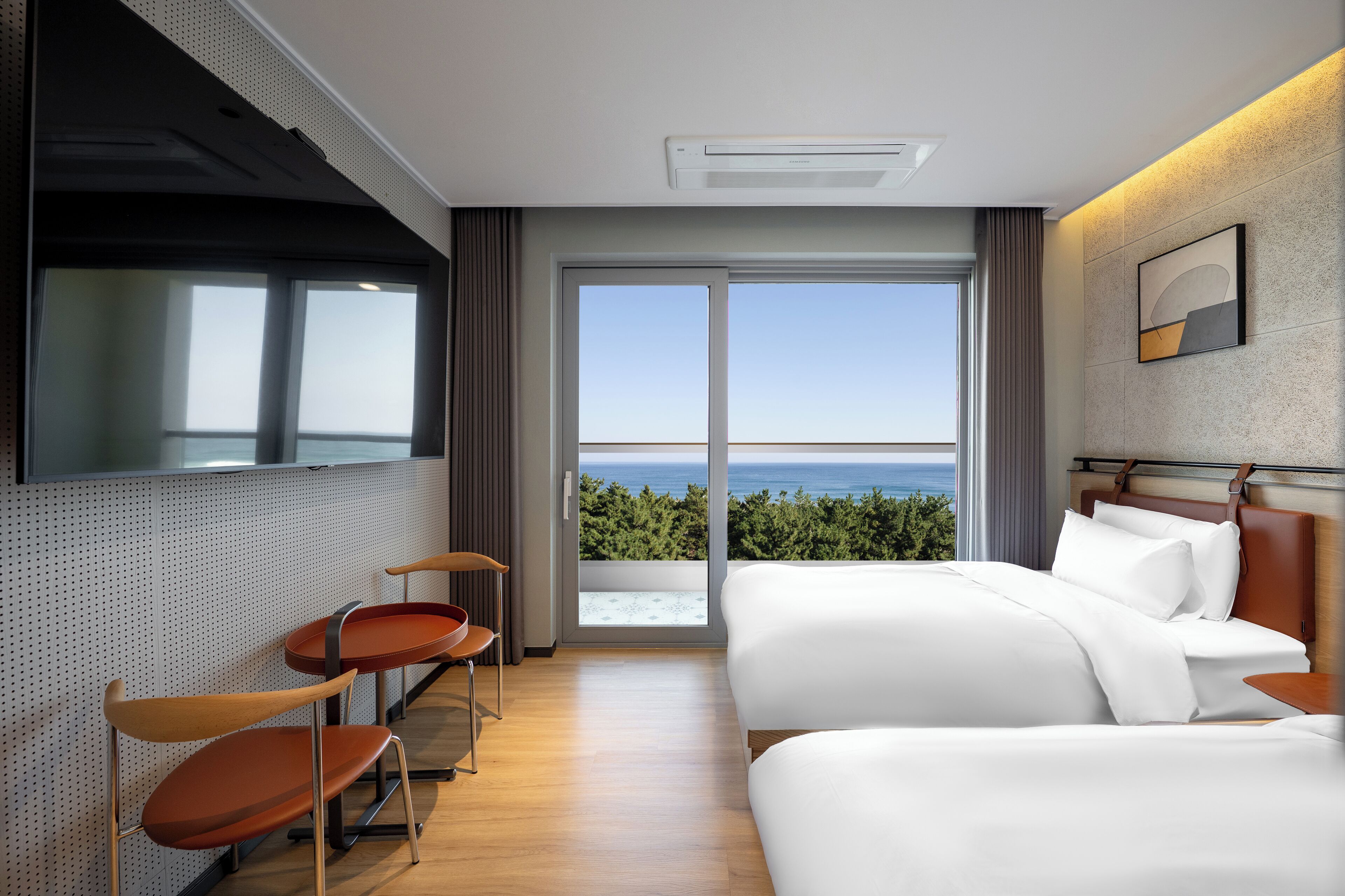 Quarto de hotel com cama, televisão na parede, uma mesinha e uma cadeira.