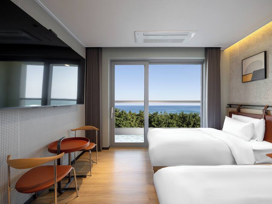 Quarto de hotel com cama, televisão na parede, uma mesinha e uma cadeira.