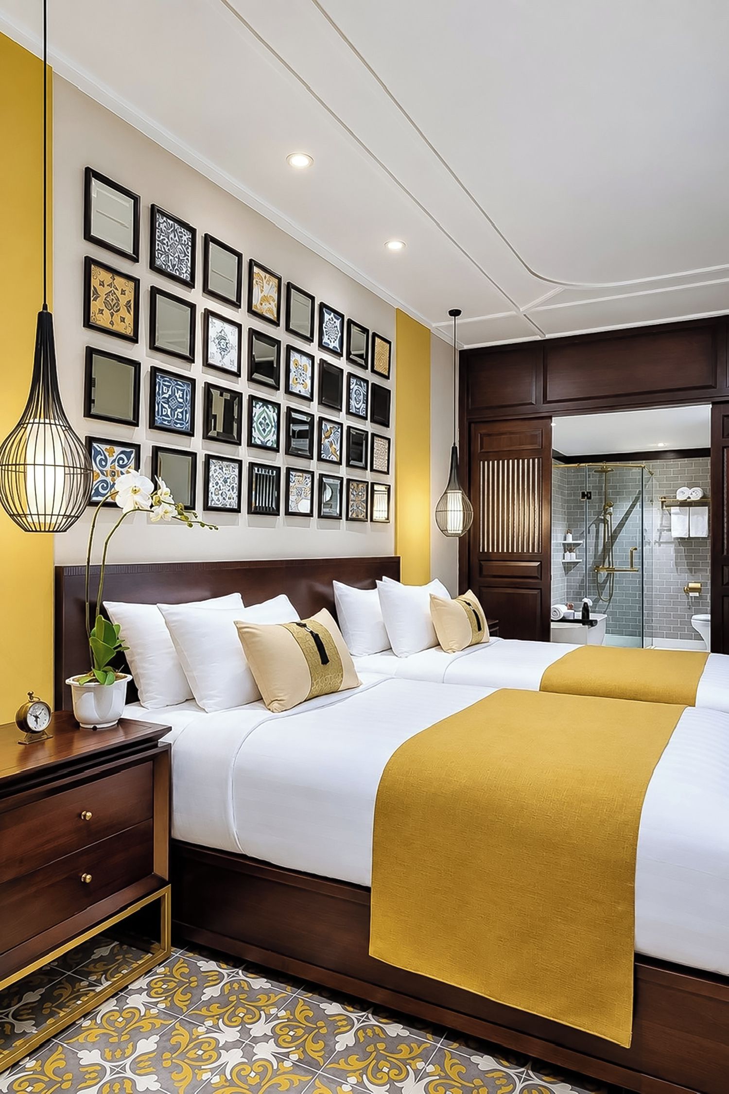 Quarto de hotel com uma cama grande, mesa de cabeceira, parede com obras de arte emolduradas e banheiro com chuveiro e vaso sanitário.