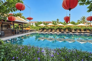 Piscina com espreguiçadeiras e guarda-sóis, cercada por vegetação e lanternas vermelhas.