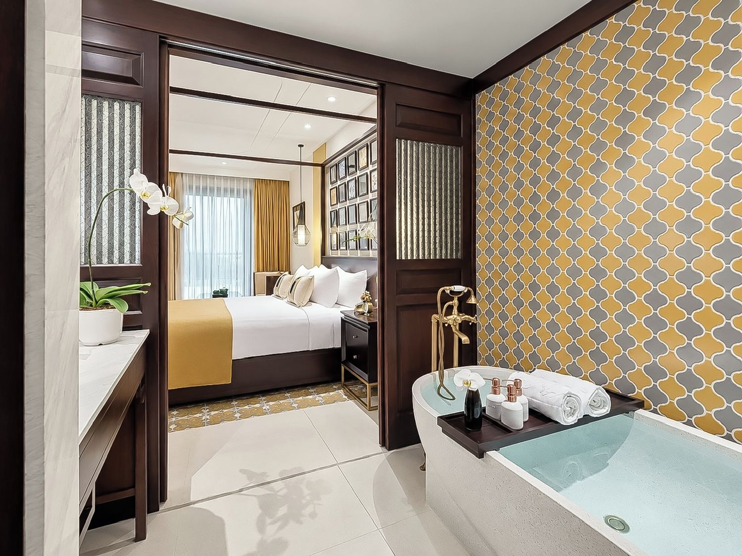 Quarto de hotel com cama, banheiro com banheira, toucador com espelho e planta em vaso.