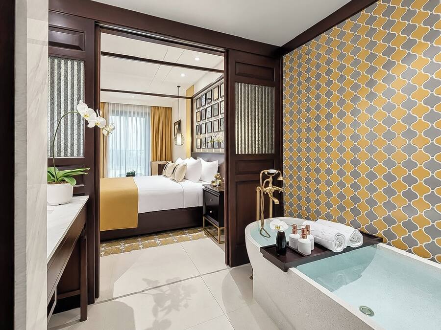 Quarto de hotel com cama, banheiro com banheira, toucador com espelho e planta em vaso.