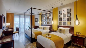 Quarto de hotel com duas camas, uma mesa com um laptop, uma cadeira, uma mesinha de cabeceira com abajur, e vista para a varanda.
