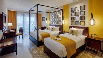 Quarto de hotel com duas camas, uma mesa com um laptop, uma cadeira, uma mesinha de cabeceira com abajur, e vista para a varanda.
