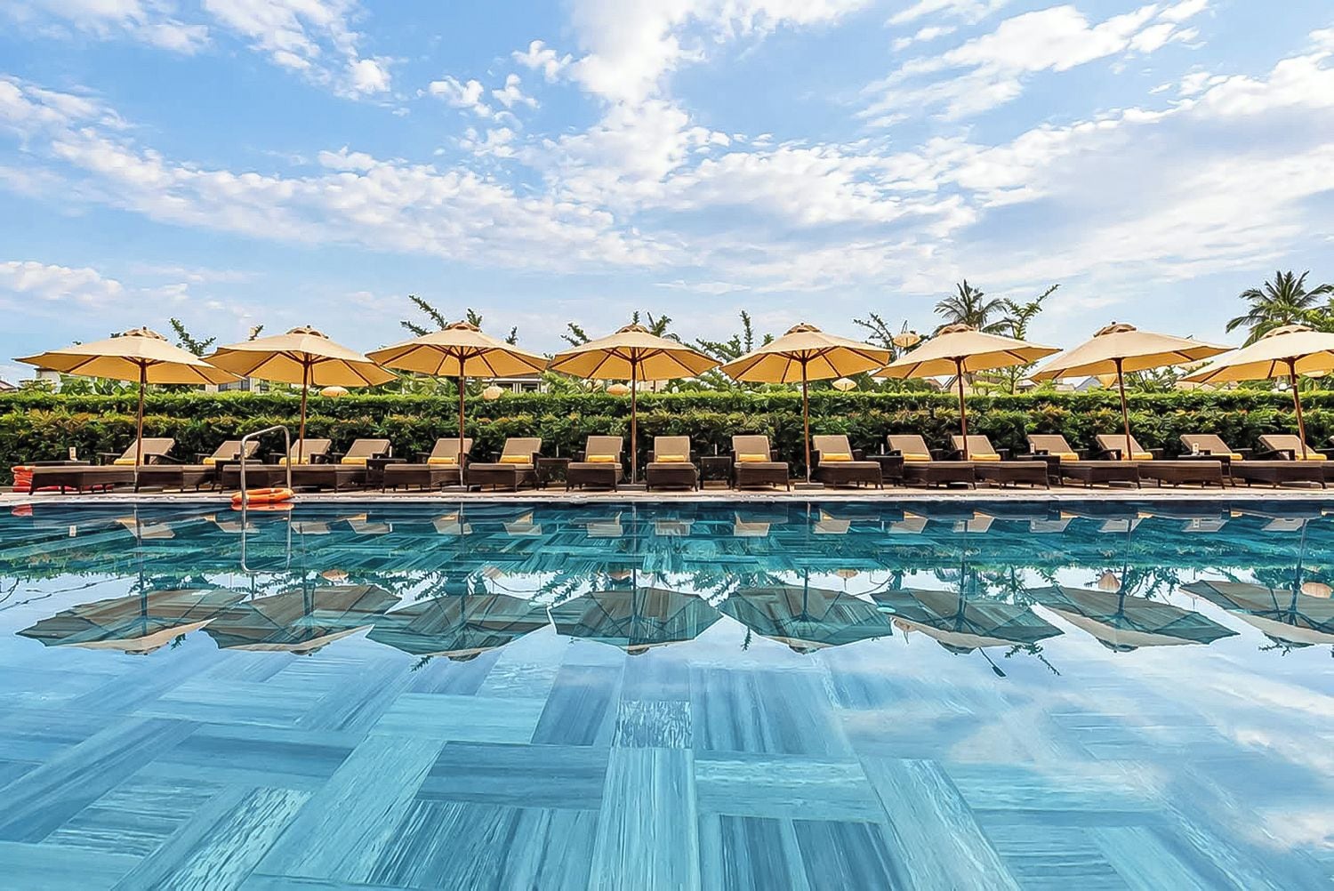 Área da piscina com espreguiçadeiras e guarda-sóis, refletindo o céu e a água.