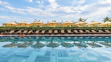 Área da piscina com espreguiçadeiras e guarda-sóis, refletindo o céu e a água.