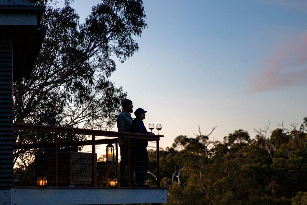 Um casal numa varanda com vista para árvores e um pôr do sol.