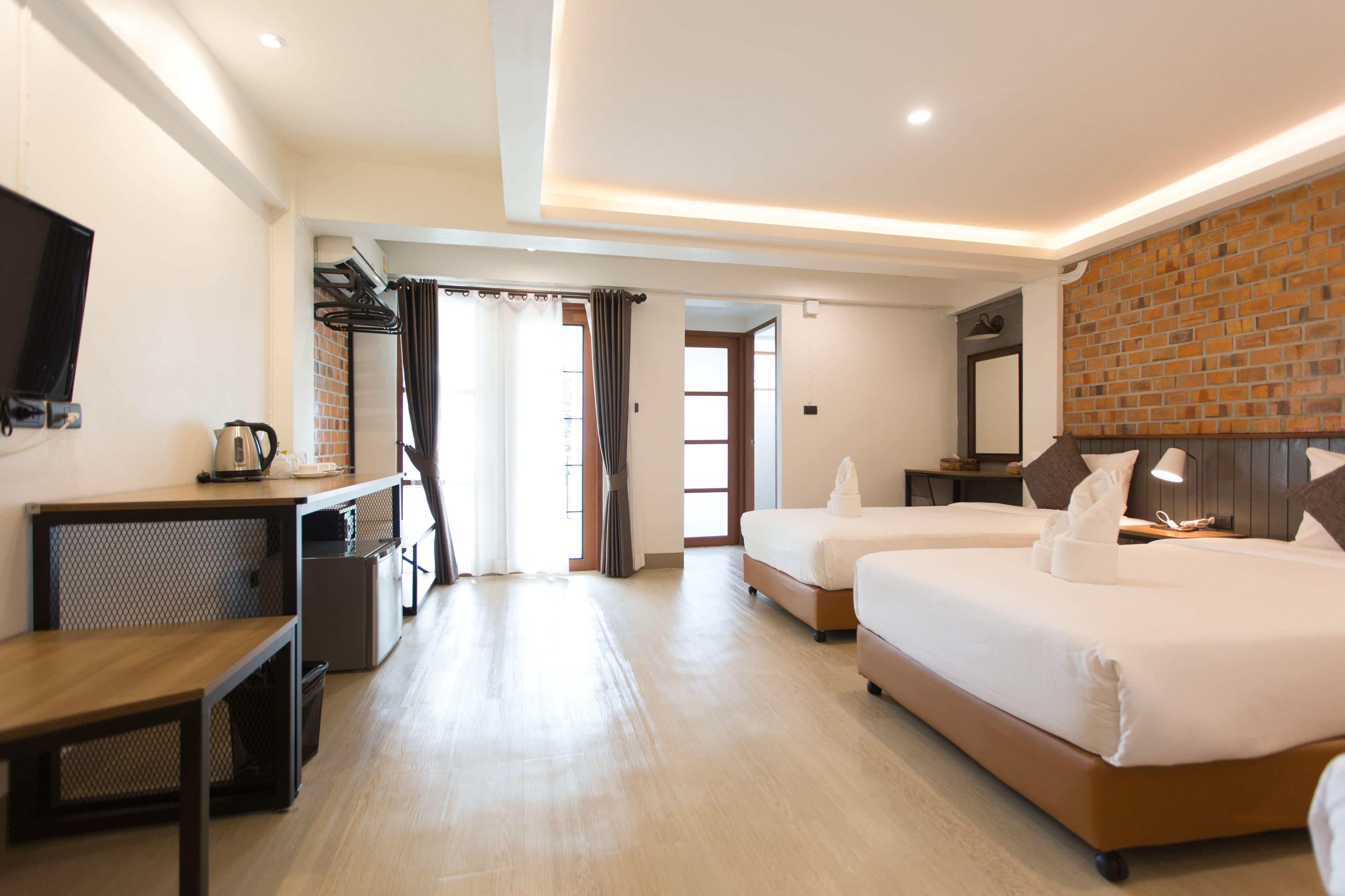 Quarto de hotel com duas camas, uma escrivaninha, uma televisão e uma parede de tijolos.