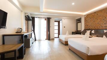 Quarto de hotel com duas camas, uma escrivaninha, uma televisão e uma parede de tijolos.
